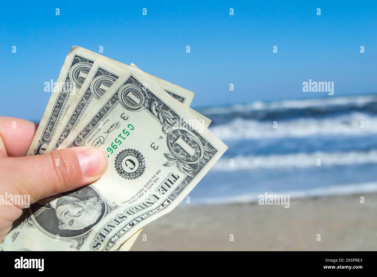 Person holding three paper dollar bills on background of sea and sea ...