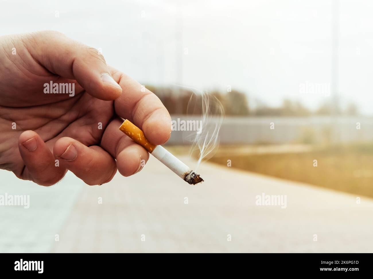 The man's hand holds a lit cigarette. Cigarettes are harmful to health ...