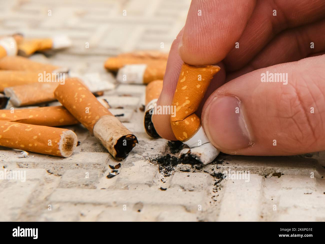 The man's hand extinguishes a lit cigarette. Cigarettes are harmful to ...