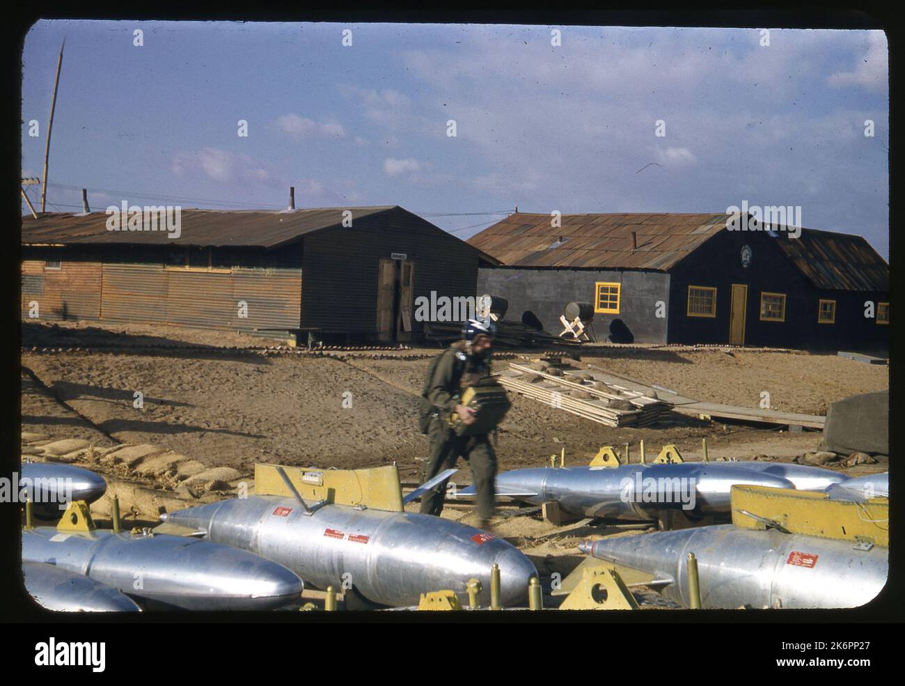 A pilot in flight gear walks past various types of drop tanks at an air ...