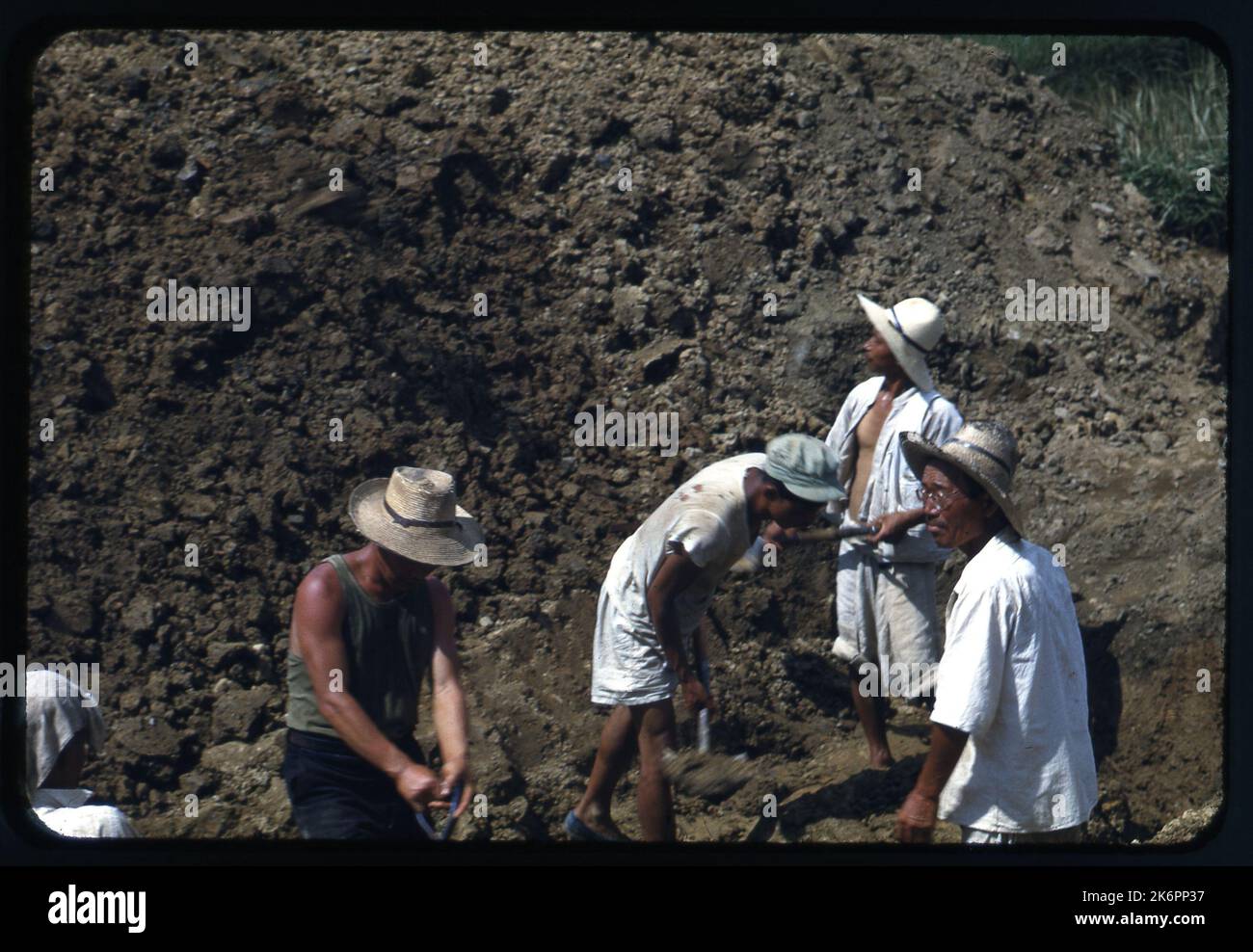 Four natives dig a hole in mud. Large pile of dirt in background.. Four ...