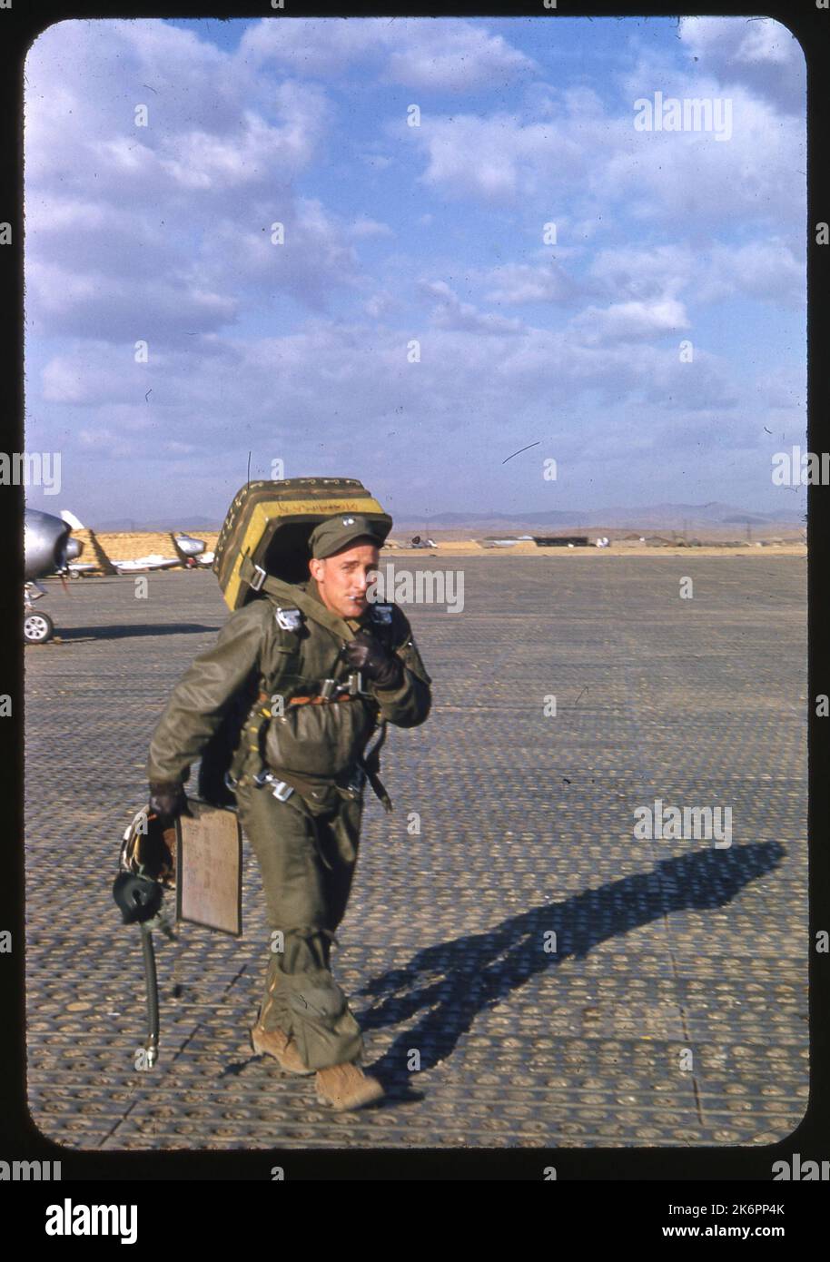 A pilot carrying his flight gear and smoking a cigarette walks by ...