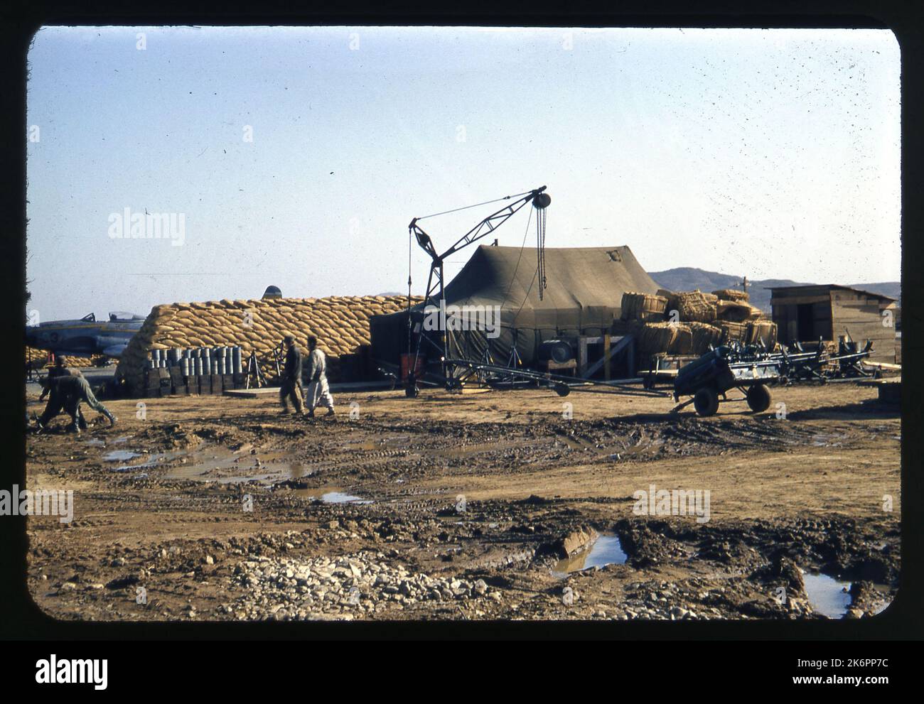Two personnel walk across a muddy field at an air base somewhere in ...