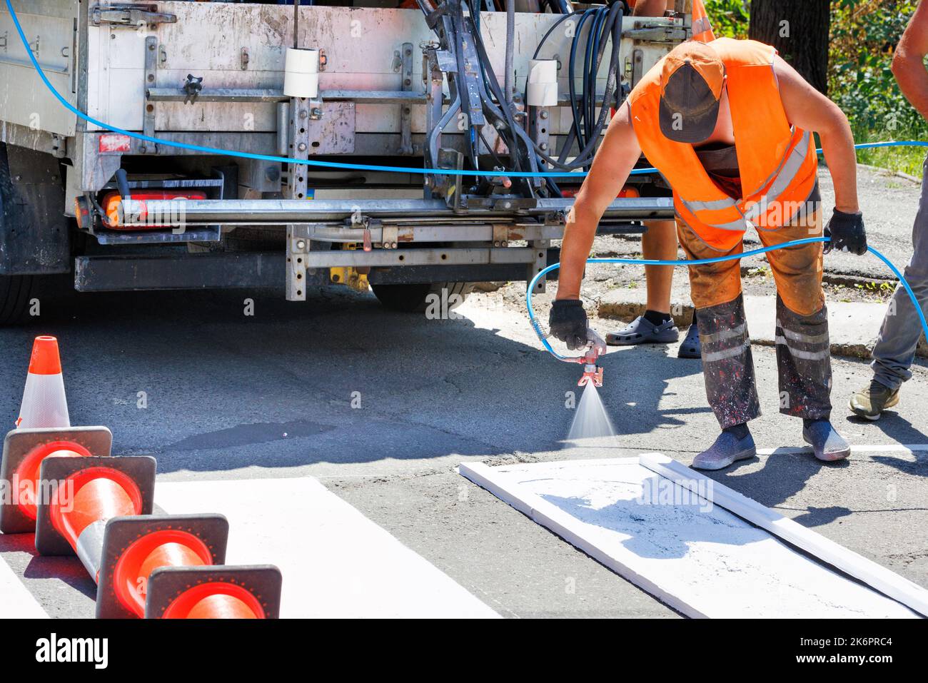 A road worker using a paint sprayer applies white road markings to a ...