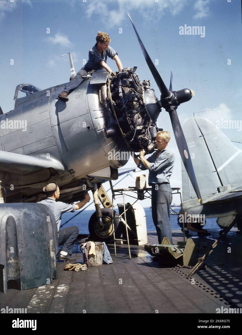 "Mechanics overhaul engine of F6F on carrier in Pacific. On cowling is ...
