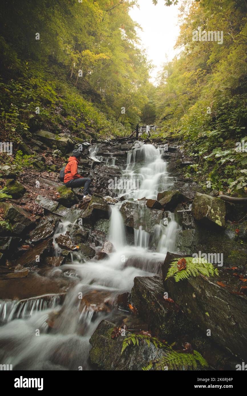 Hiker in a red jacket sits next to waterfalls in the untouched nature ...