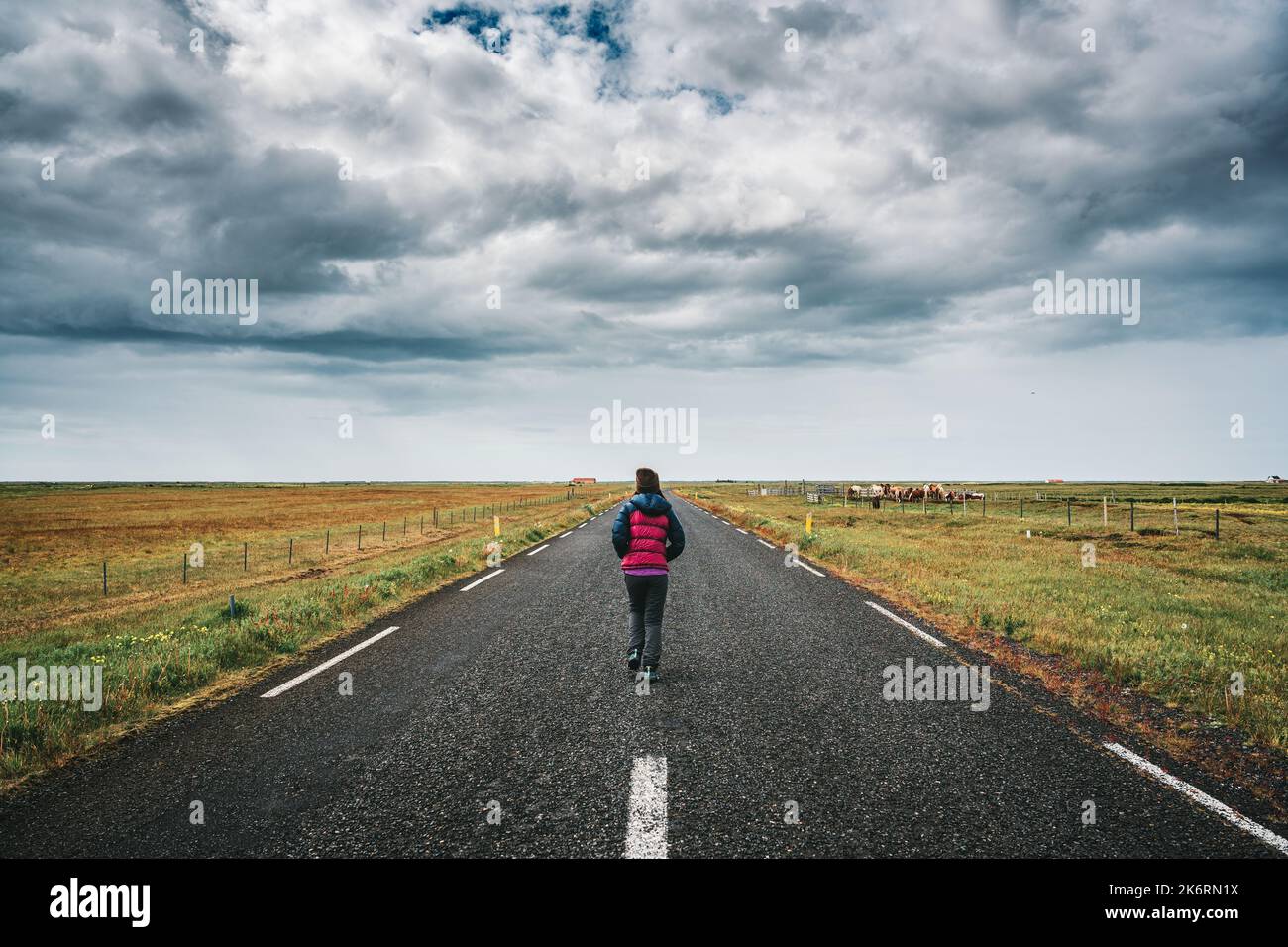 One female tourist running on straight road through farmland and stormy ...