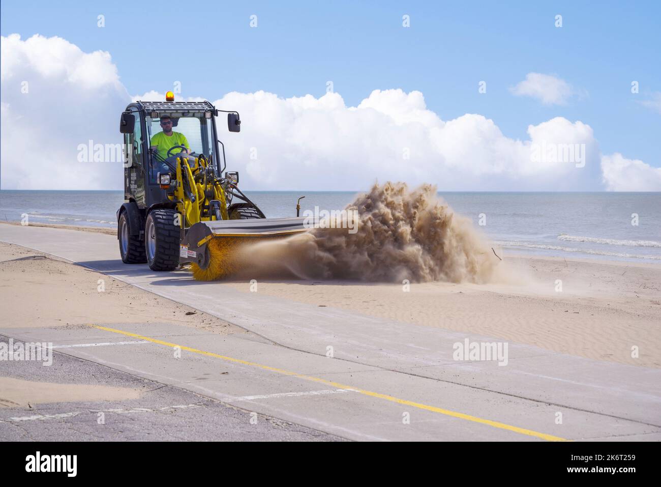 Park maintenance worker on tractor sweeping sand off concrete walk at ...