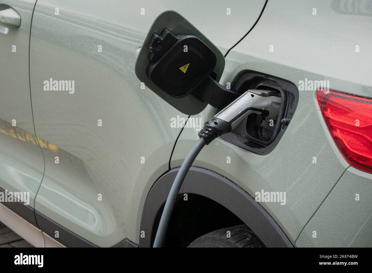 Close up of power supply plugged into gray electric car being charged ...