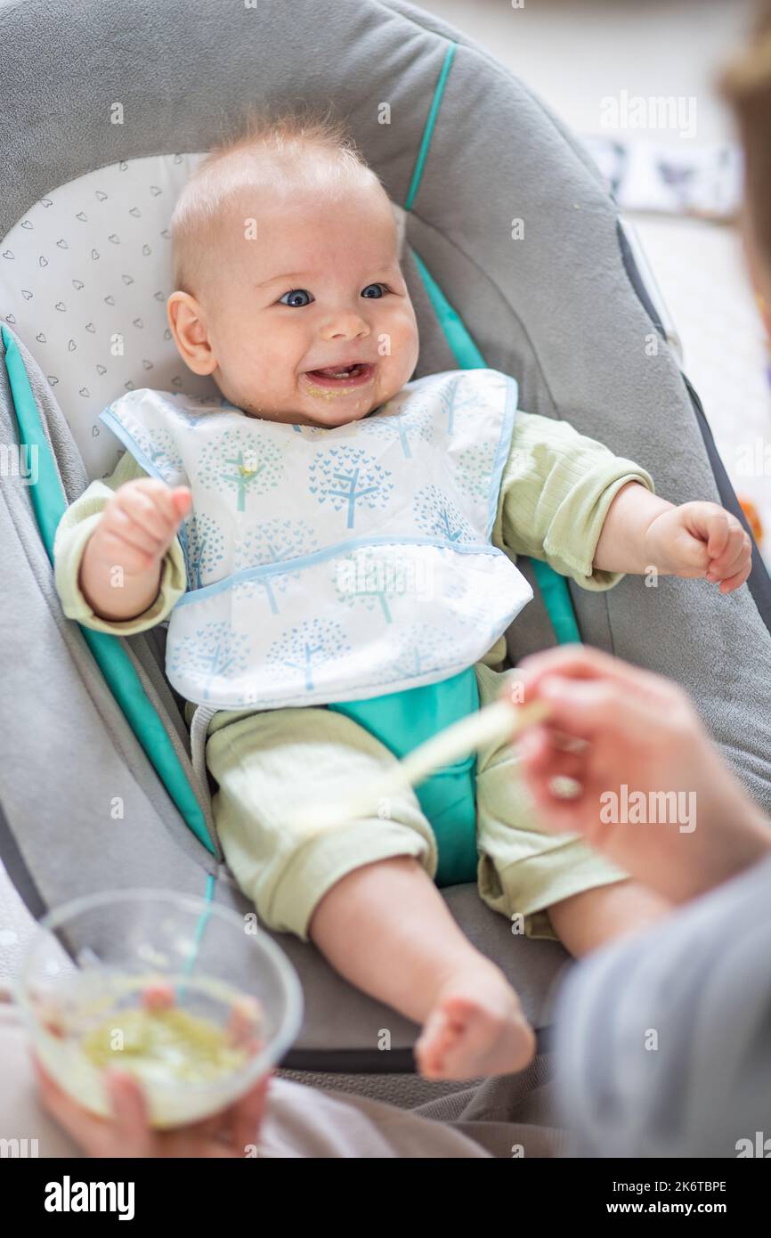 Mother spoon feeding her baby boy infant child in baby chair with fruit ...