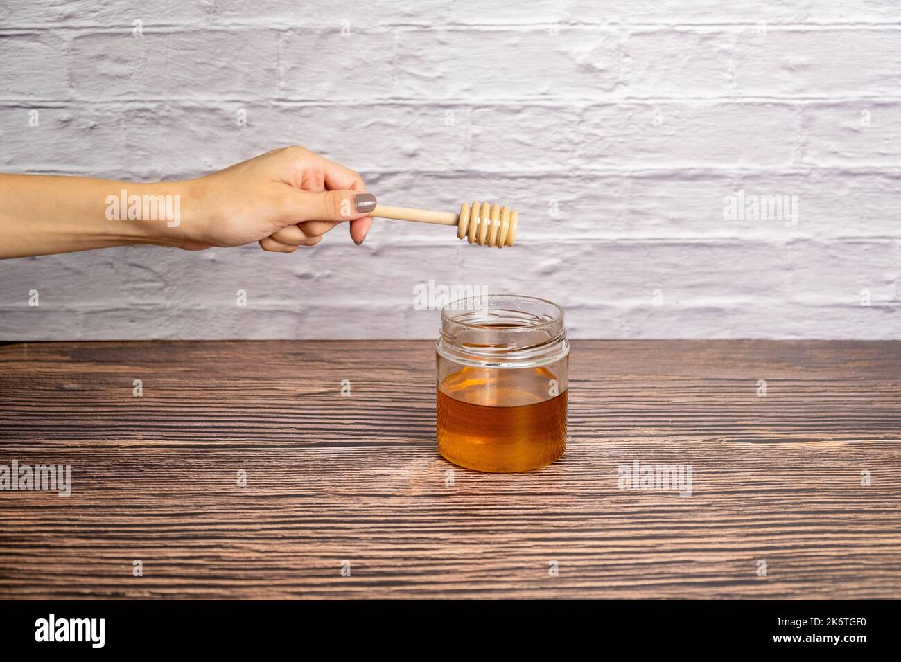 Pot of honey and wooden stick isolated white brick wall Stock Photo - Alamy