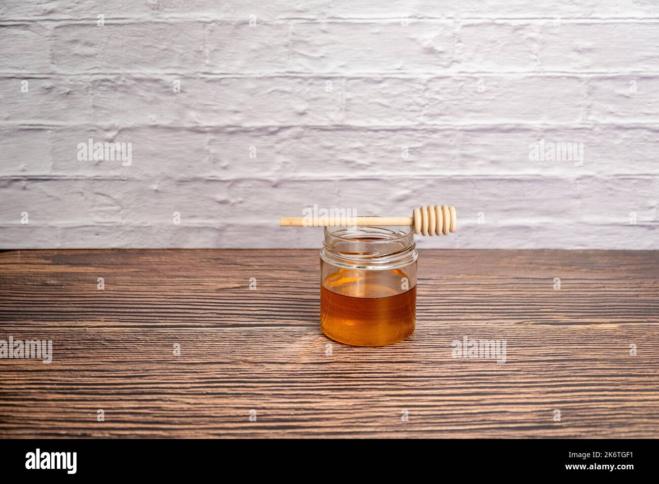 Pot of honey and wooden stick isolated white brick wall Stock Photo - Alamy