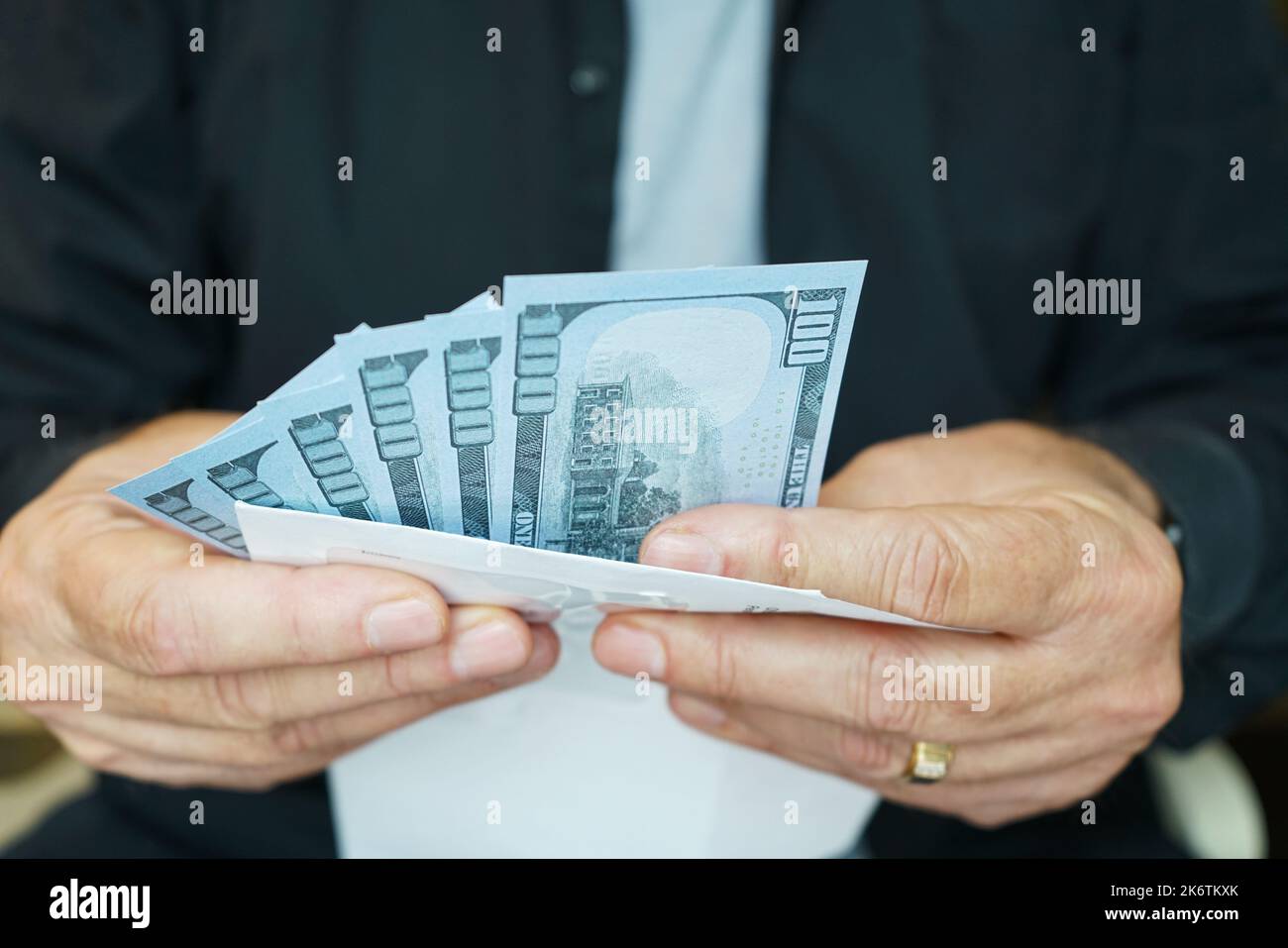 Close up of man holding cash and envelope with 100 dollar bills visible ...