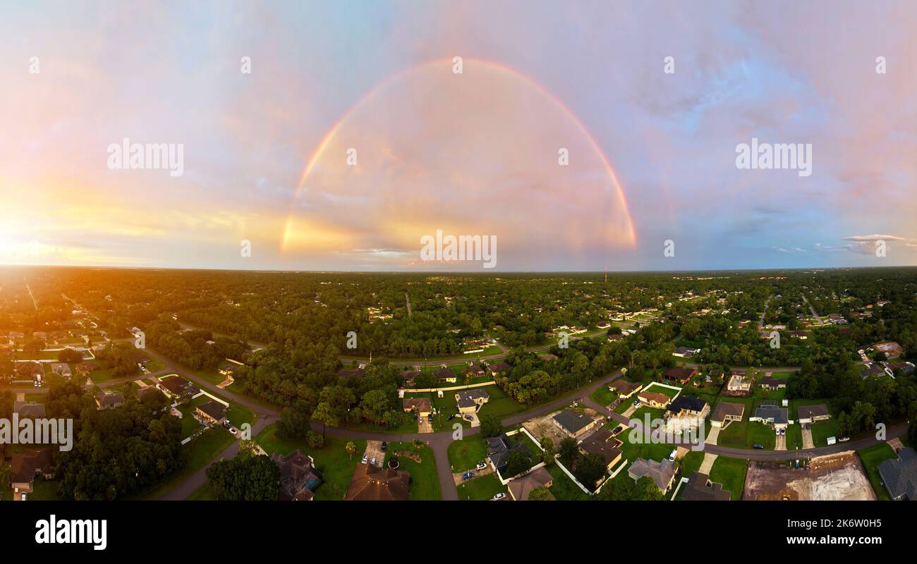 Colorful round rainbow over rural town suburbs against blue evening sky ...