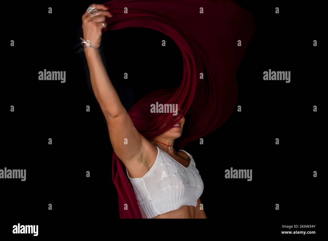 Woman moving a red cloth over her head against a black background ...