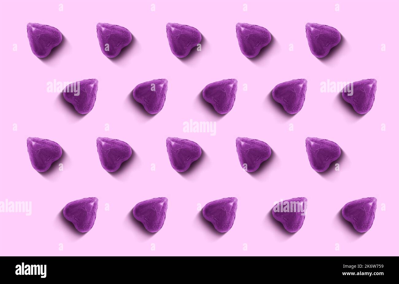 A repeating pattern of heart-shaped candies wrapped in purple foil on a ...