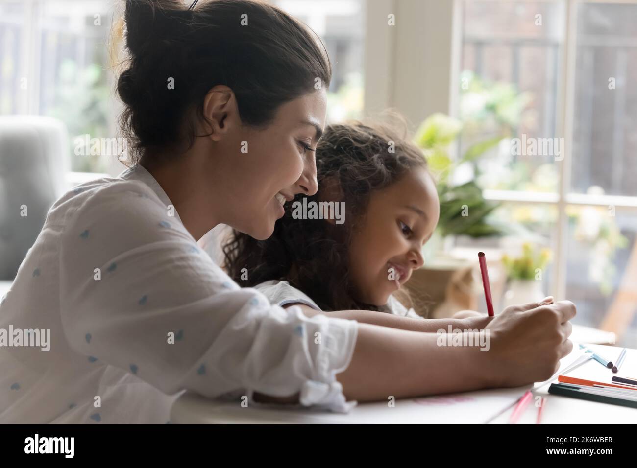 Indian mum little daughter drawing in sketchbook with colored pencils ...