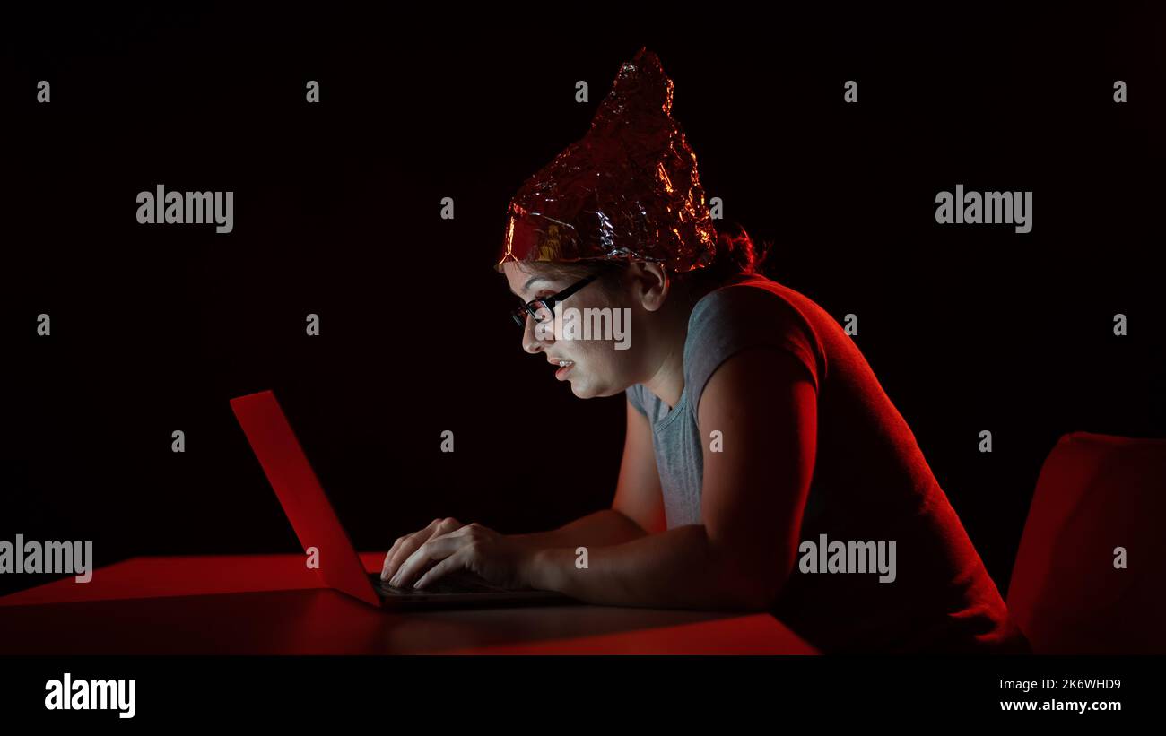 Paranoid caucasian woman typing on a computer wearing a tinfoil cap ...