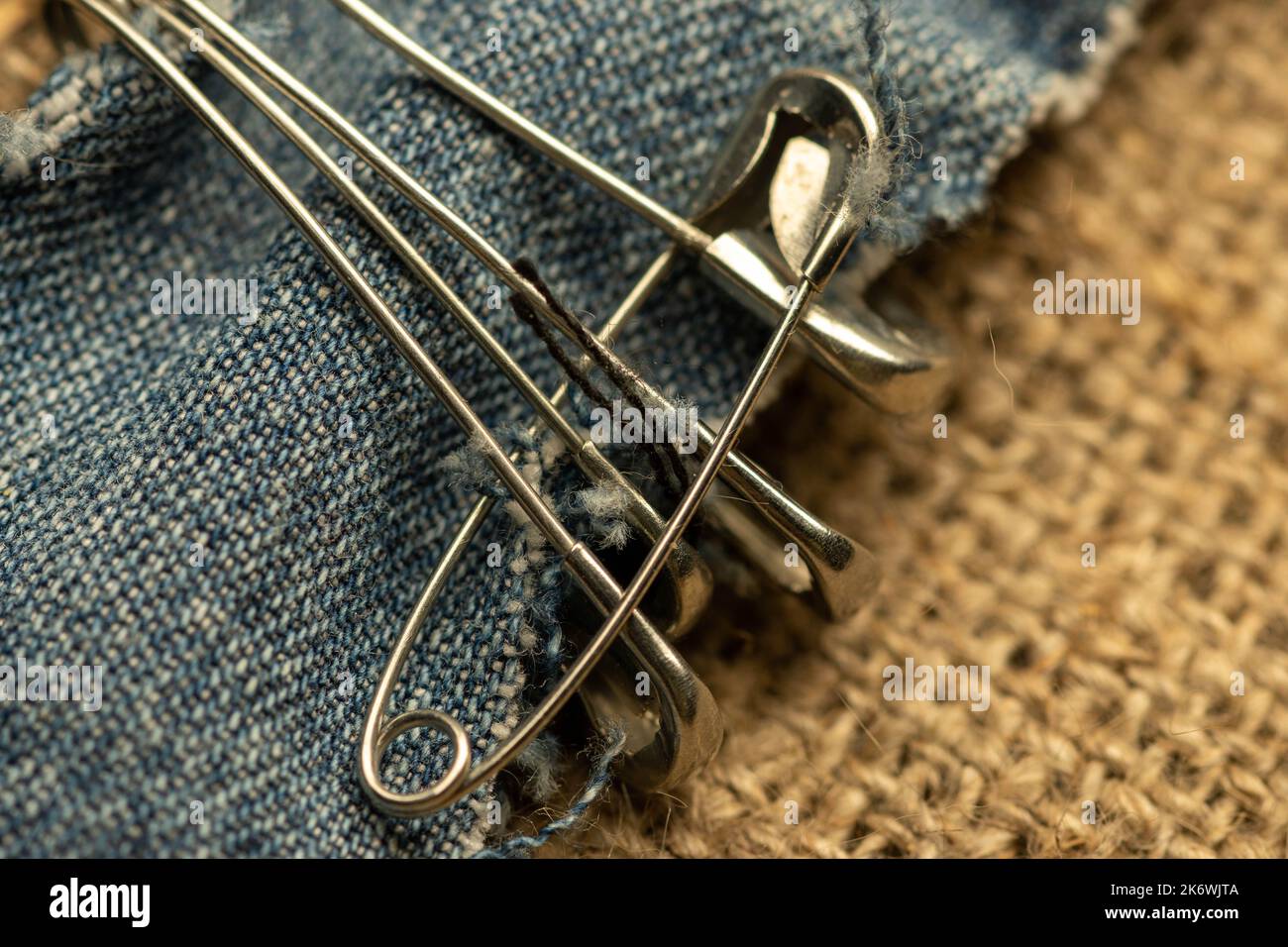 Safety pins on a strip of denim against a homespun fabric with a rough ...