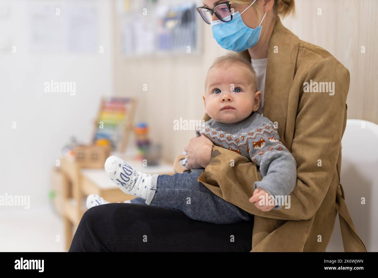 Mother holding infant baby boy in her lap, sitting and waiting in front ...