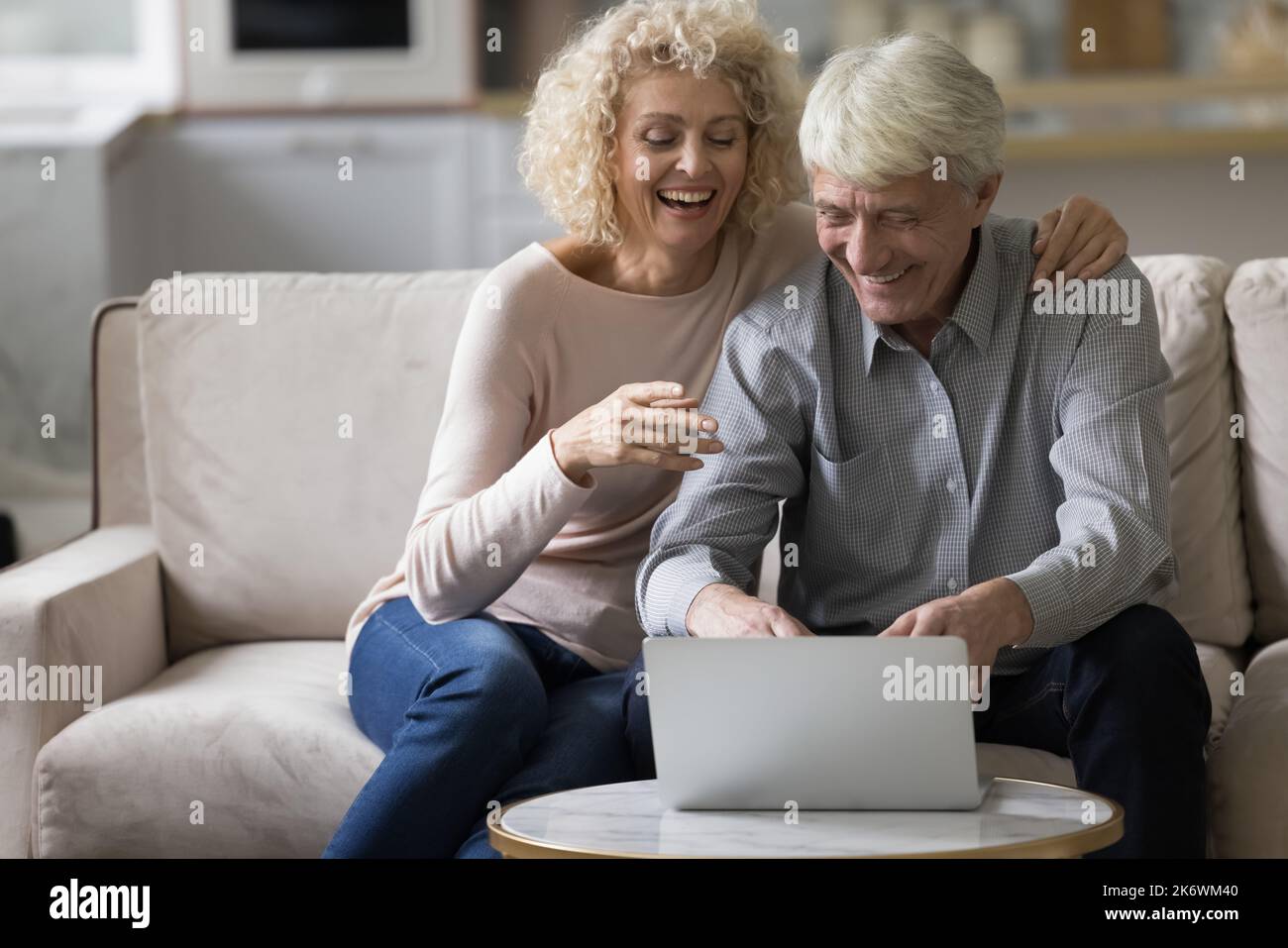Older couple sit on sofa laughing staring at laptop screen Stock Photo ...