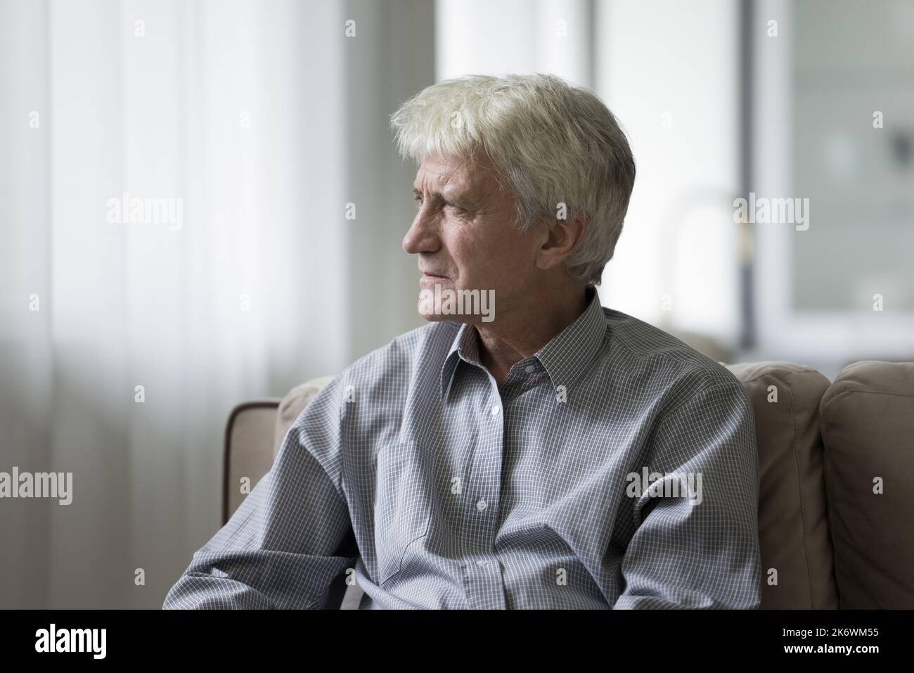 Gloomy elderly man sits on sofa staring into distance Stock Photo - Alamy
