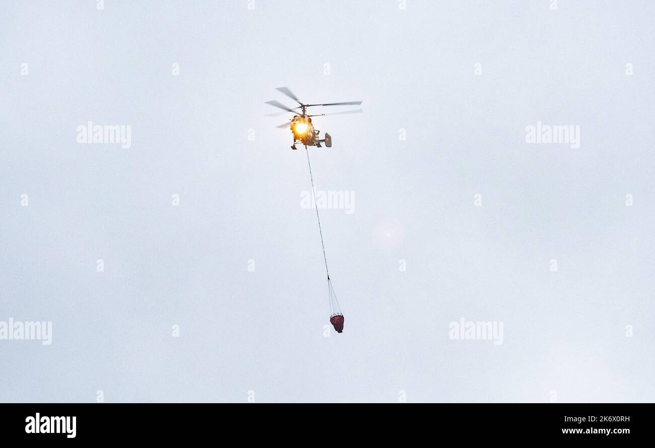 A fire helicopter carries a container of water to extinguish a fire in ...