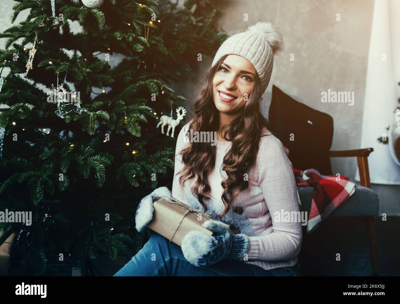 Happy young lady in hat holds gifts near the Christmas tree. New year ...