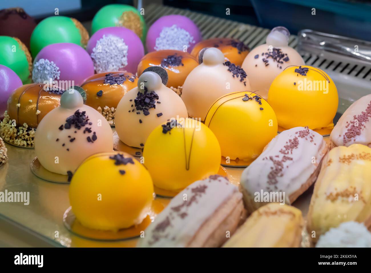 Set of multicolor mousse cakes and eclairs on counter at food market ...