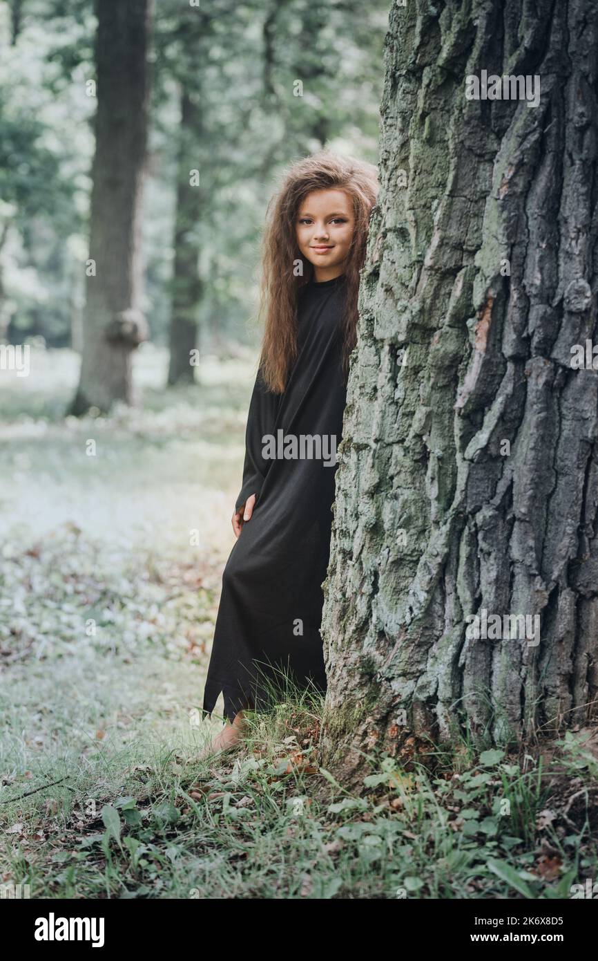 A little girl in a witch costume in a forest near a tree, Halloween ...