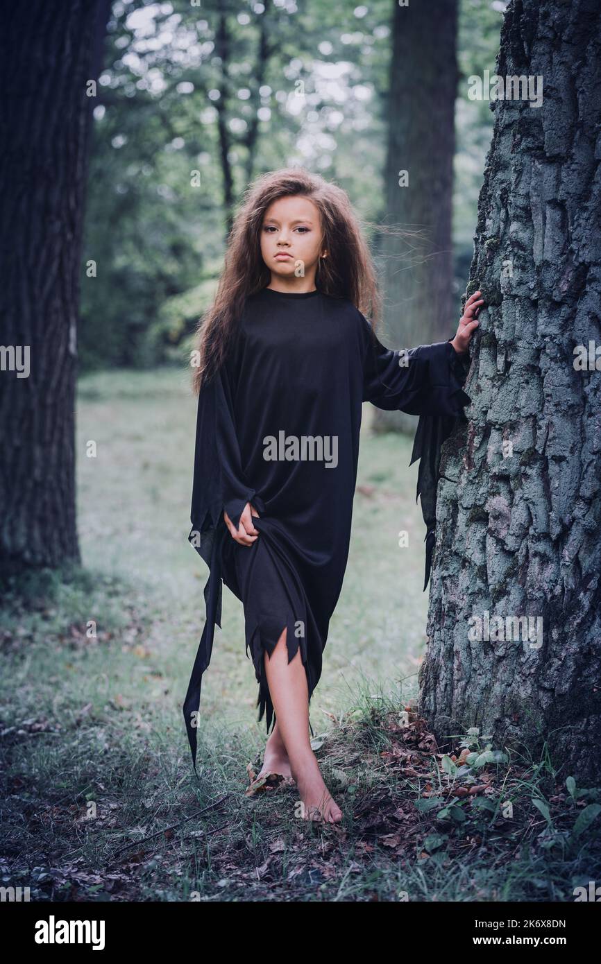 A little girl in a witch costume in a forest near a tree, Halloween ...
