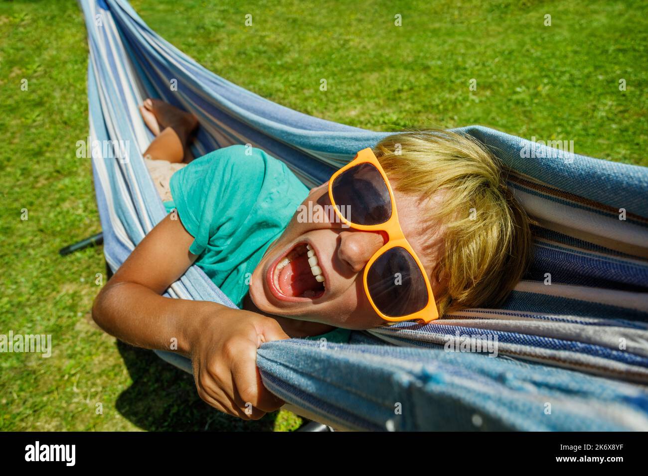 Happy screaming young boy with orange sunglasses lay in hammock Stock ...