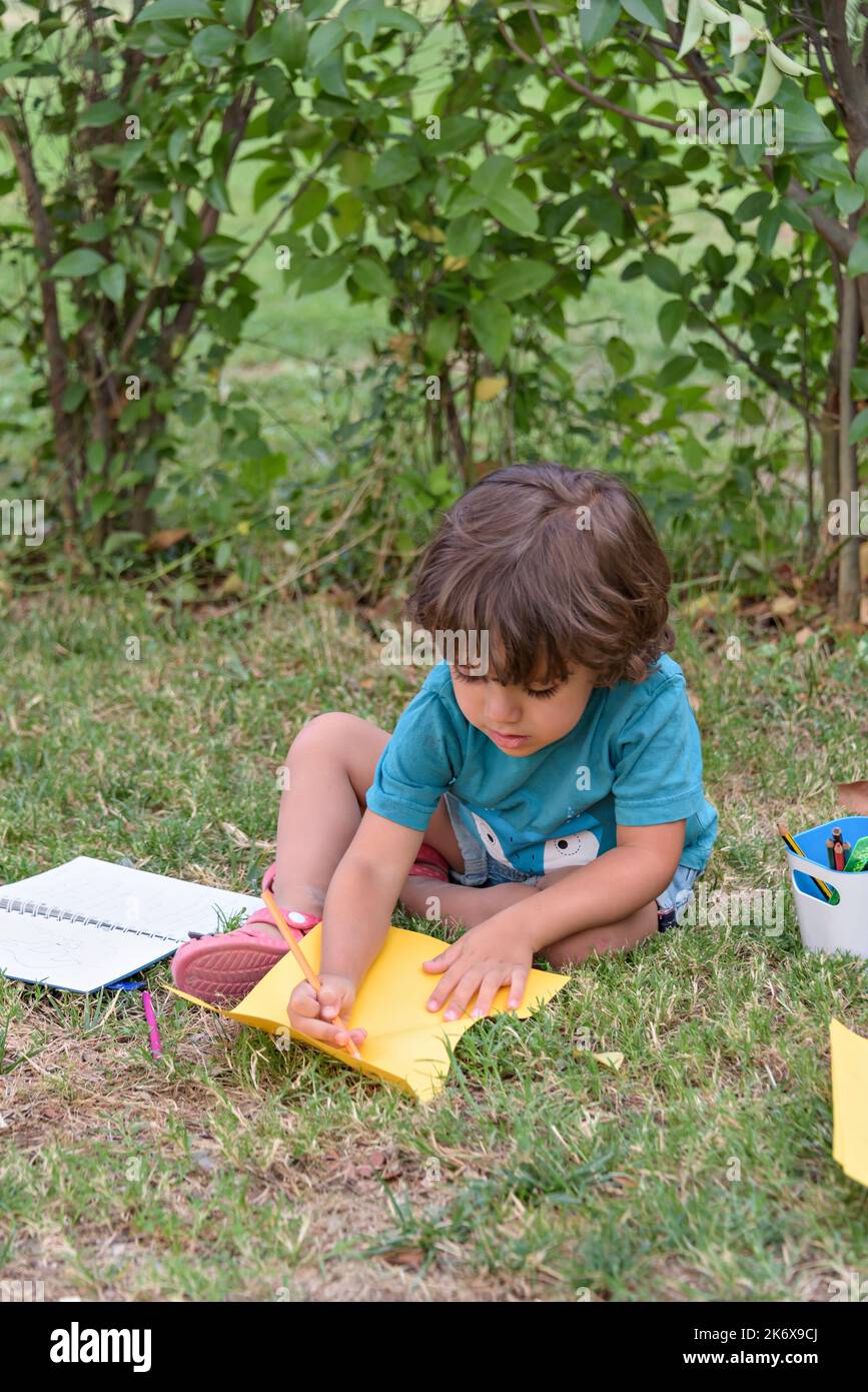 Young Caucasian school boy sitting in park outdoor doing school ...