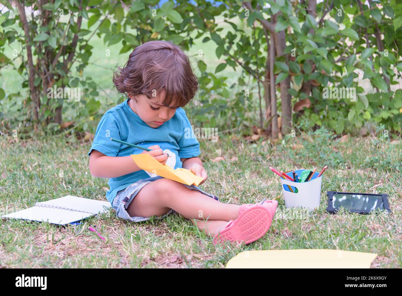 Young Caucasian school boy sitting in park outdoor doing school ...