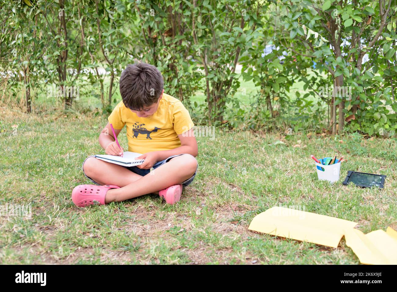 Little caucasian boy writing book with pencil in the park on sunset ...