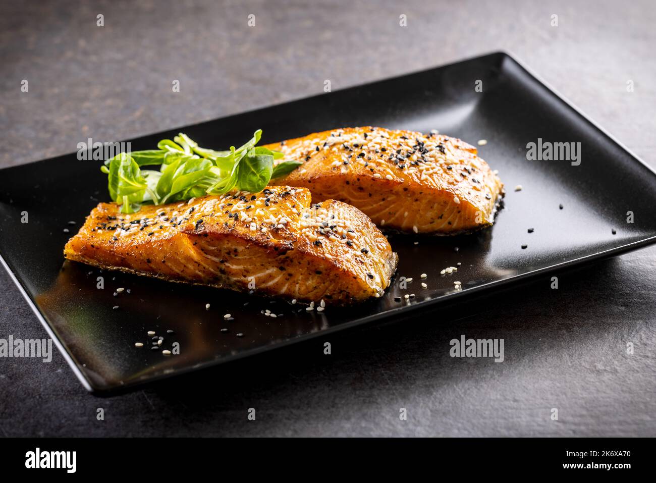 Two salmon fillets baked until crispy, sprinkled with sesame on a black ...
