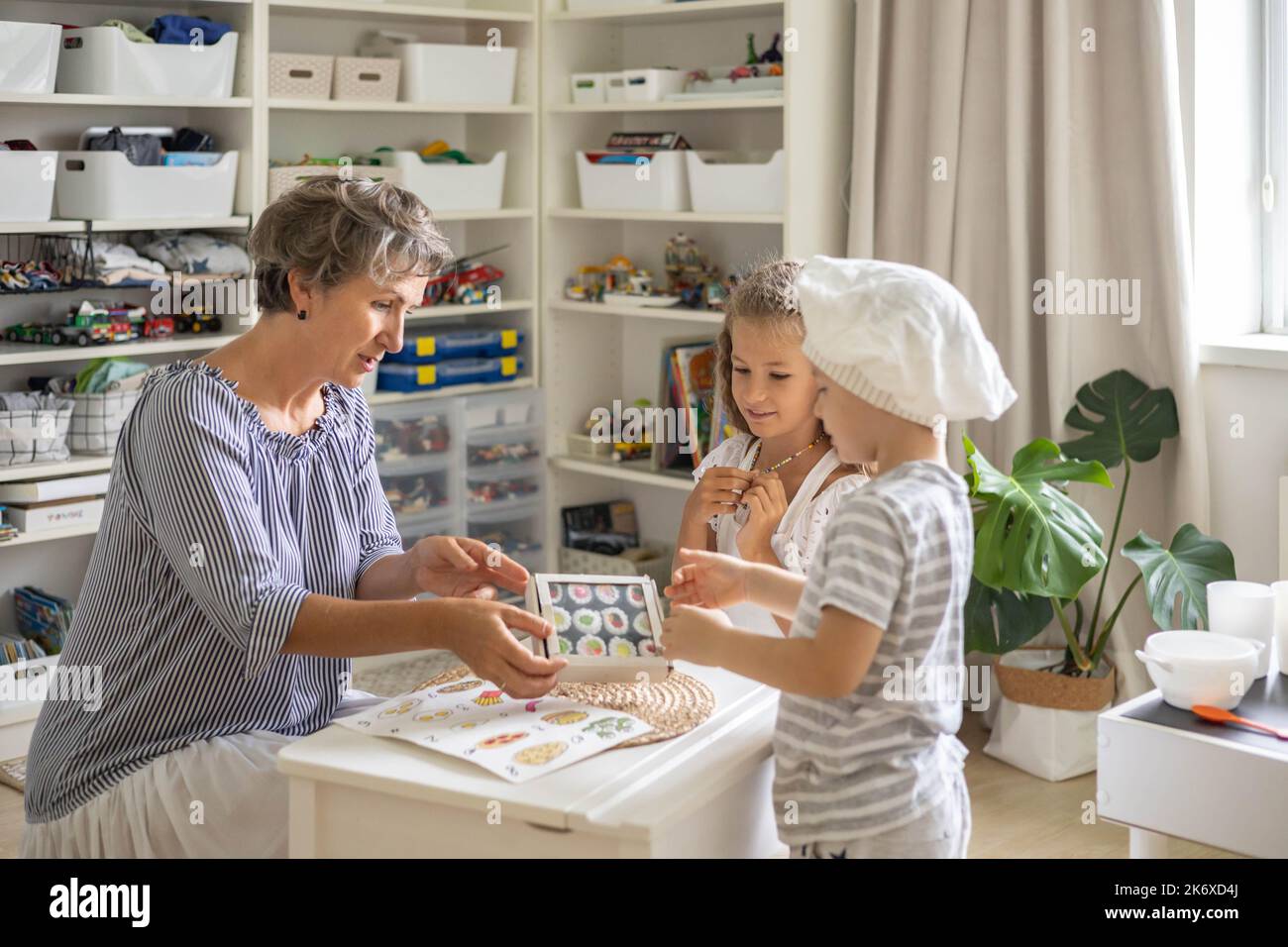 Mother and cute baby boy and girl cooking food at childish kitchen ...
