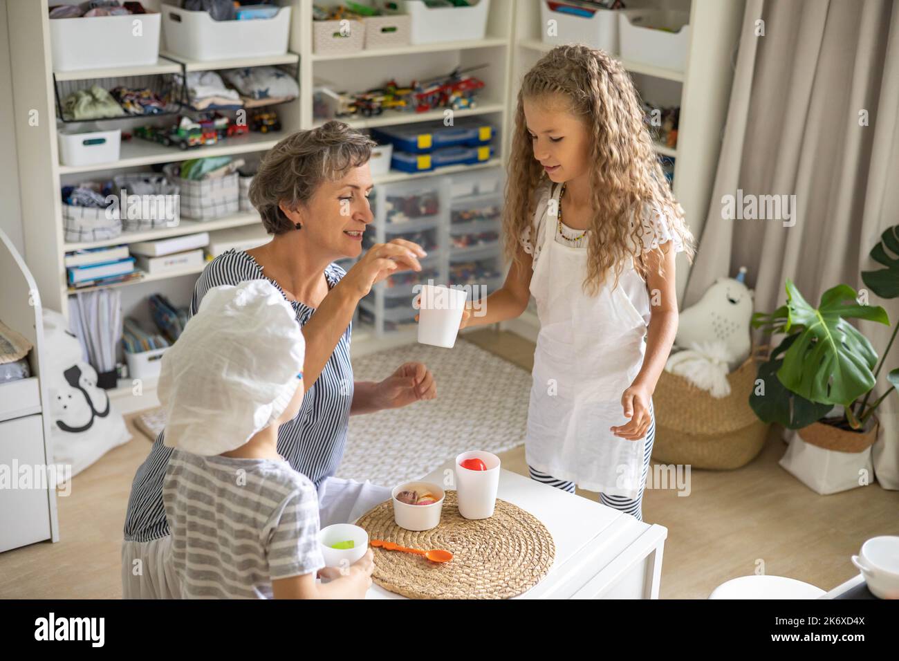 Mother and cute baby boy and girl cooking food at childish kitchen ...