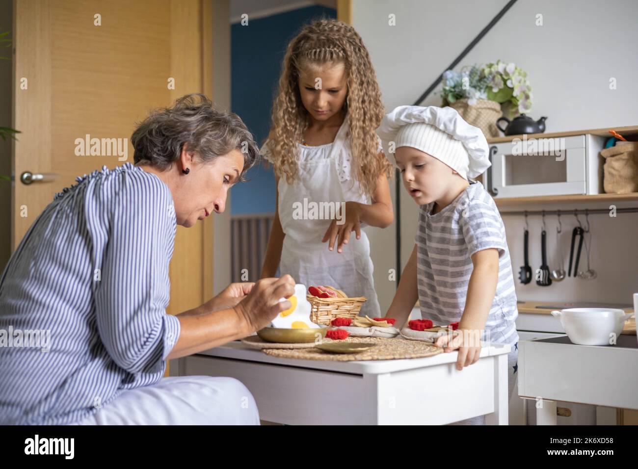 Mother and cute baby boy and girl cooking food at childish kitchen ...