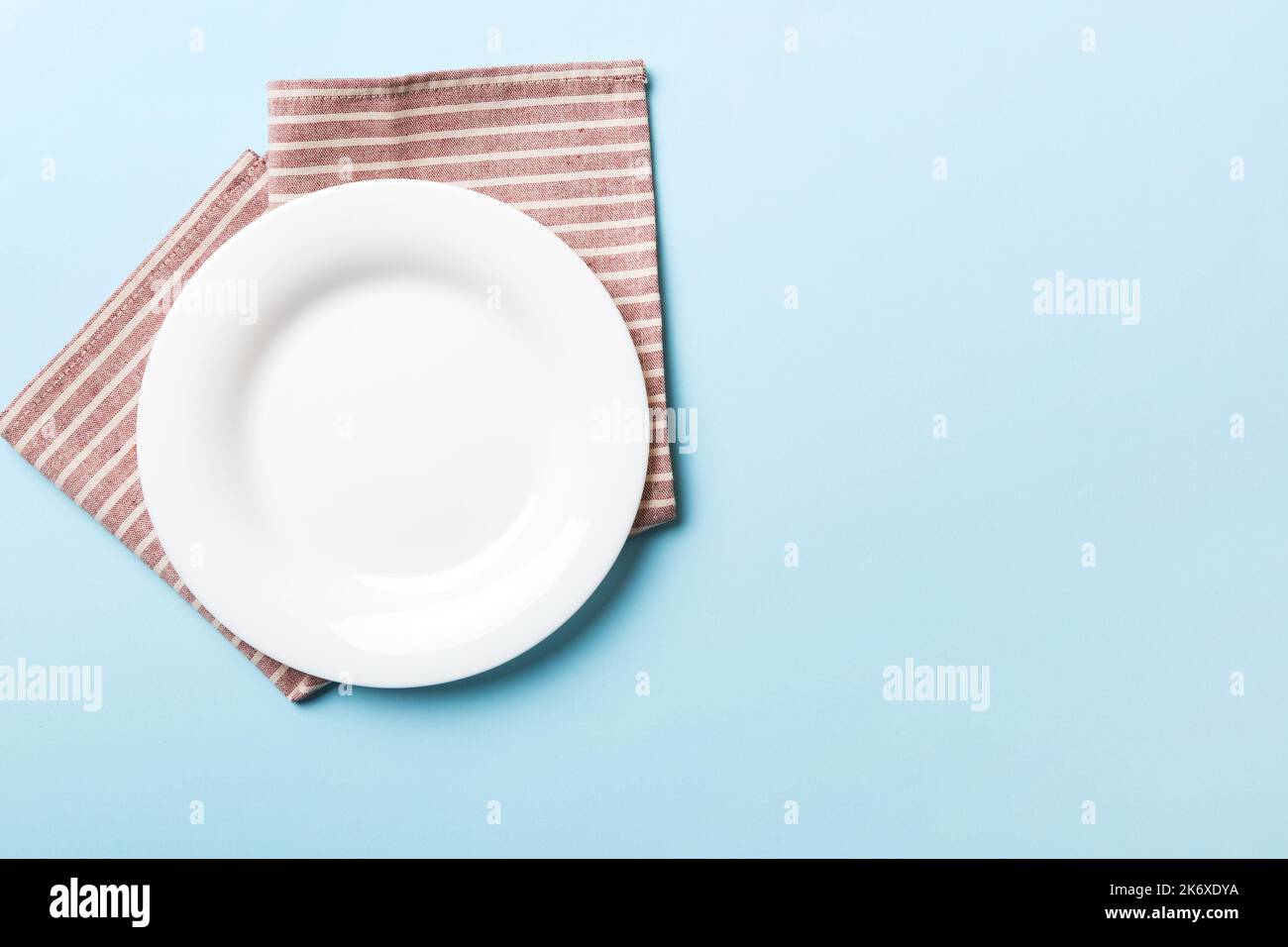 Top view on colored background empty round white plate on tablecloth ...