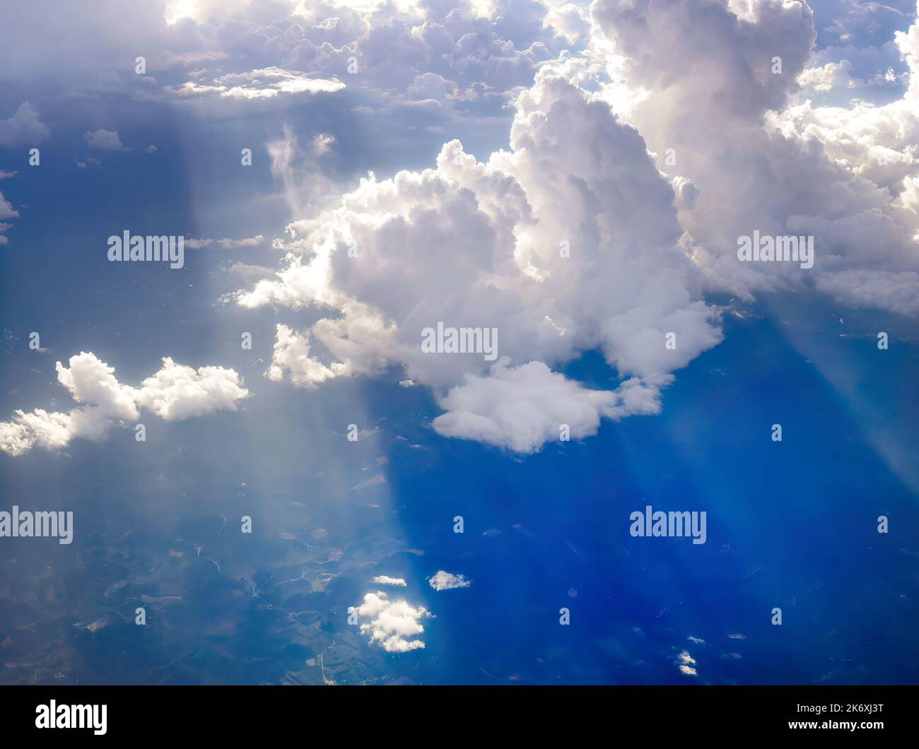Aerial view flying above dramatic fluffy clouds and sun rays piercing ...