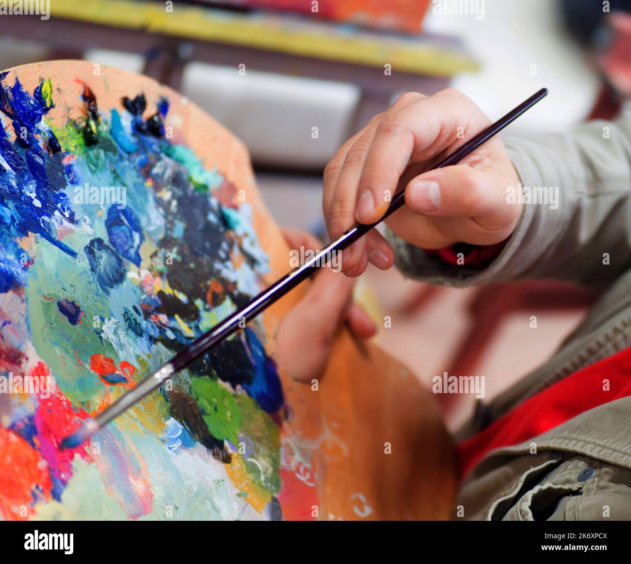 Close up of man's hand mix paints with brush in palette and painting ...