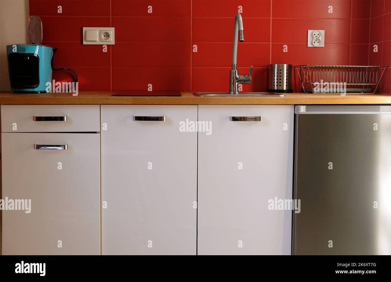row of modern white kitchen cabinets with red tile wall, woodent ...