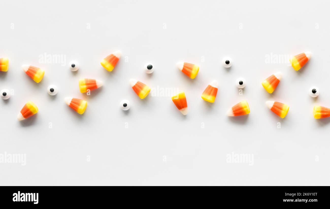 A line of candy corn and candy eyeballs, against a white background ...