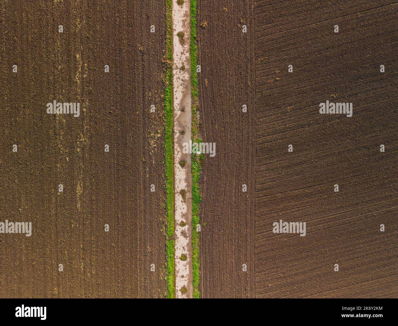 Aerial view dirt road made of concrete divides field with wet fertile ...