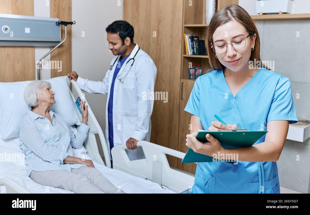 Smiling elderly patient talking with her doctor in hospital room while ...