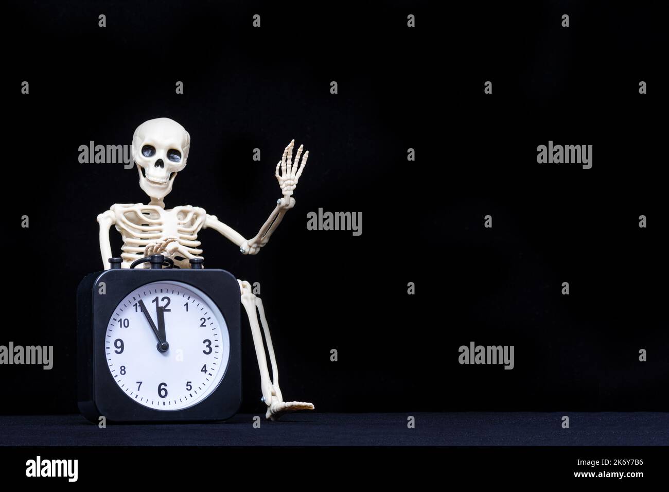 A human skeleton waving his hand, greeting holding an black alarm clock ...