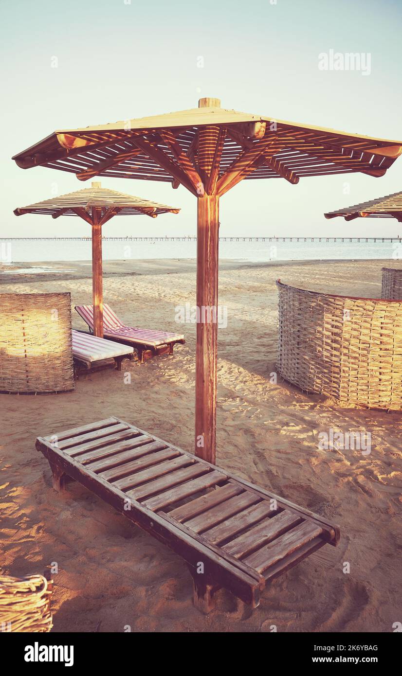 Wooden sun umbrellas, sunbeds and windscreens on beach, color toning ...