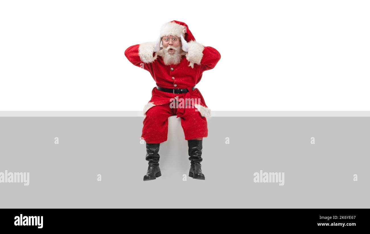 Surprised Santa Claus sitting on a blank panel isolated on white ...