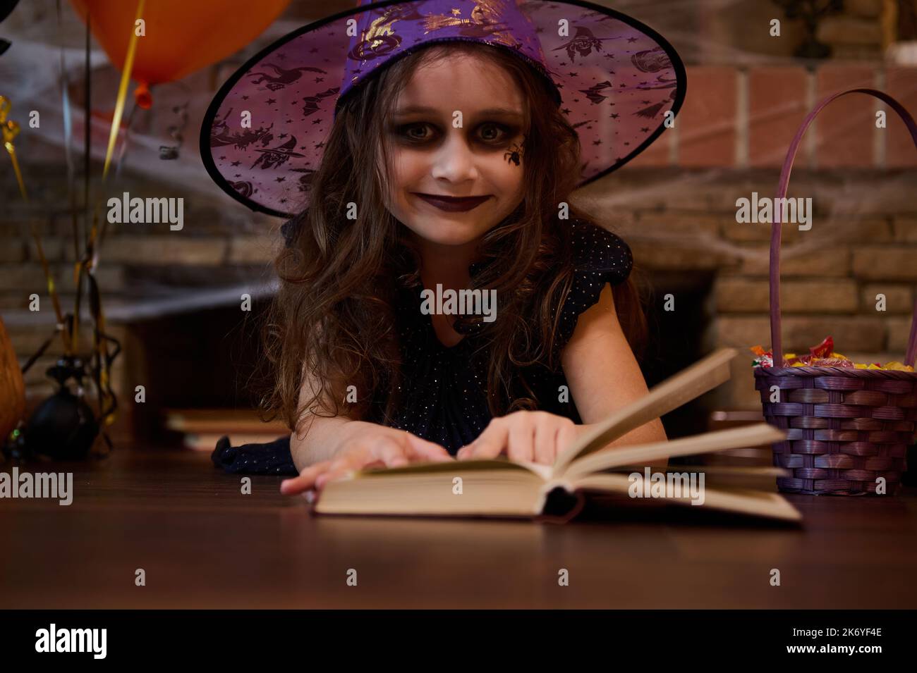 Little girl in witch carnival costume smiles at camera while reading ...